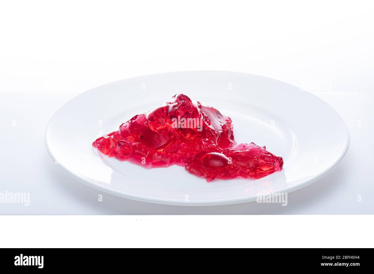 Red shapeless jelly on a white plate. Red jelly on a white background ...