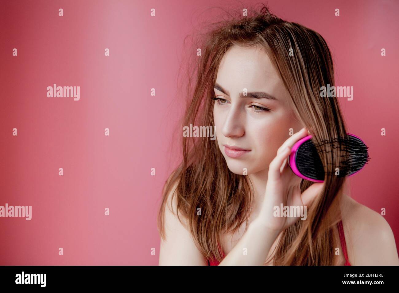 Young beautiful girl having problems while hair on pink background ...