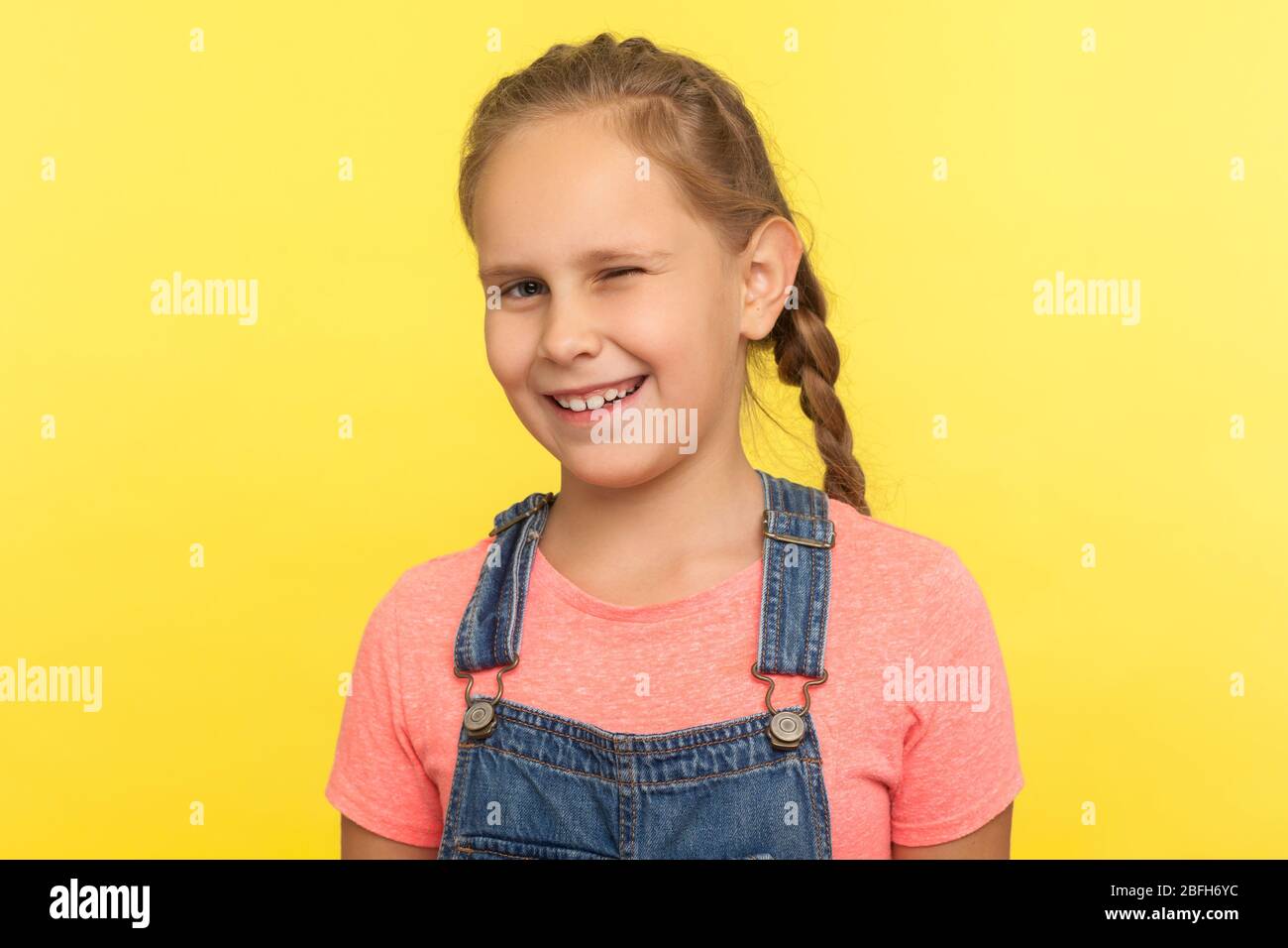 Portrait of funny charming little girl with braid in denim overalls ...