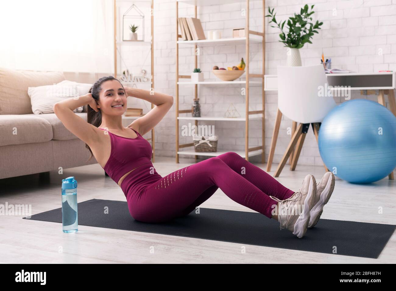 Stay at home sports. Cheerful Hispanic girl doing abs workout in light ...