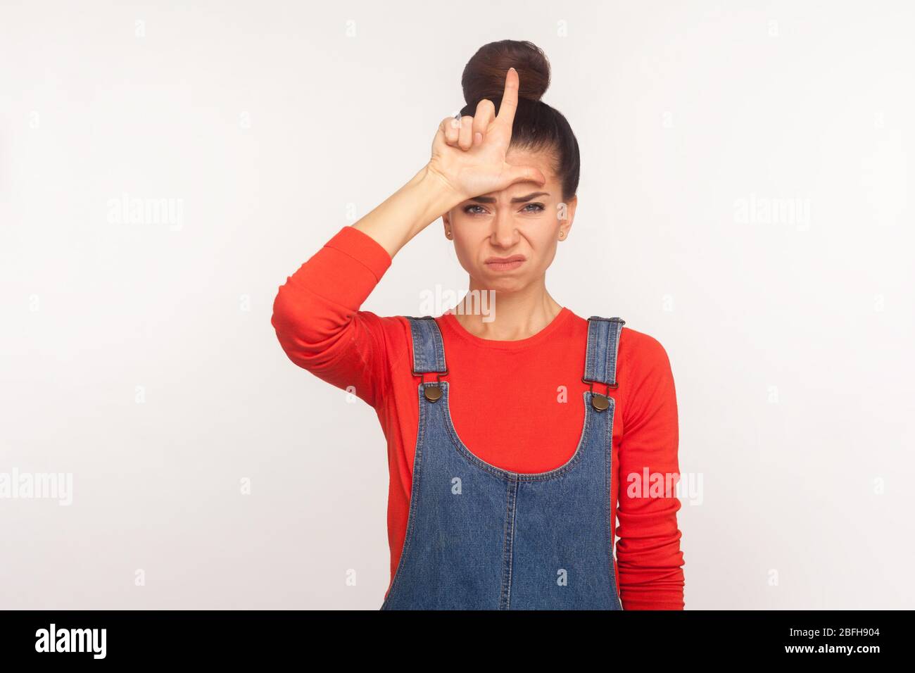 Portrait of unlucky frustrated girl with hair bun in denim overalls ...