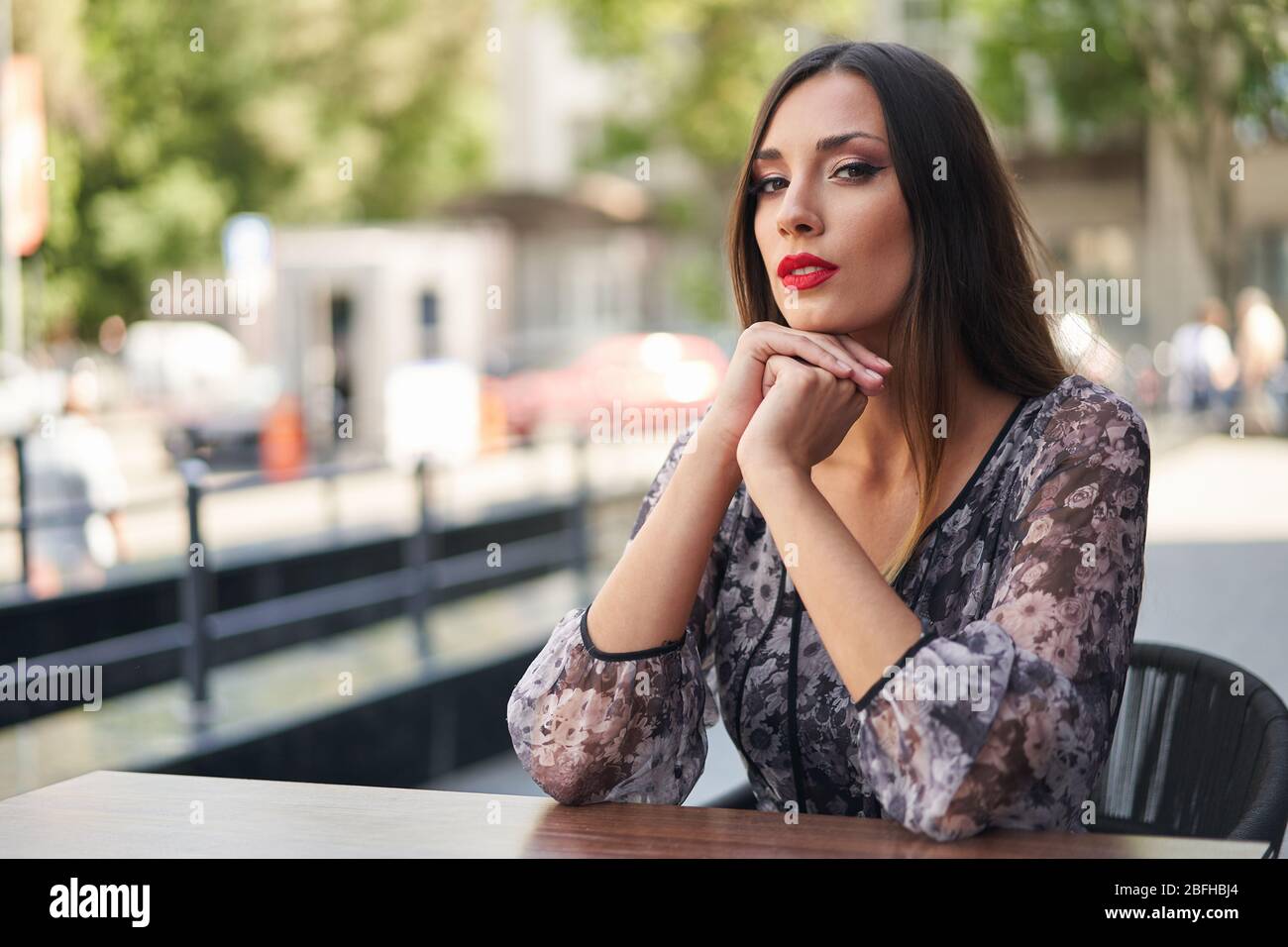 Beautiful elegant young girl with dark dyed long hair sits at a table ...