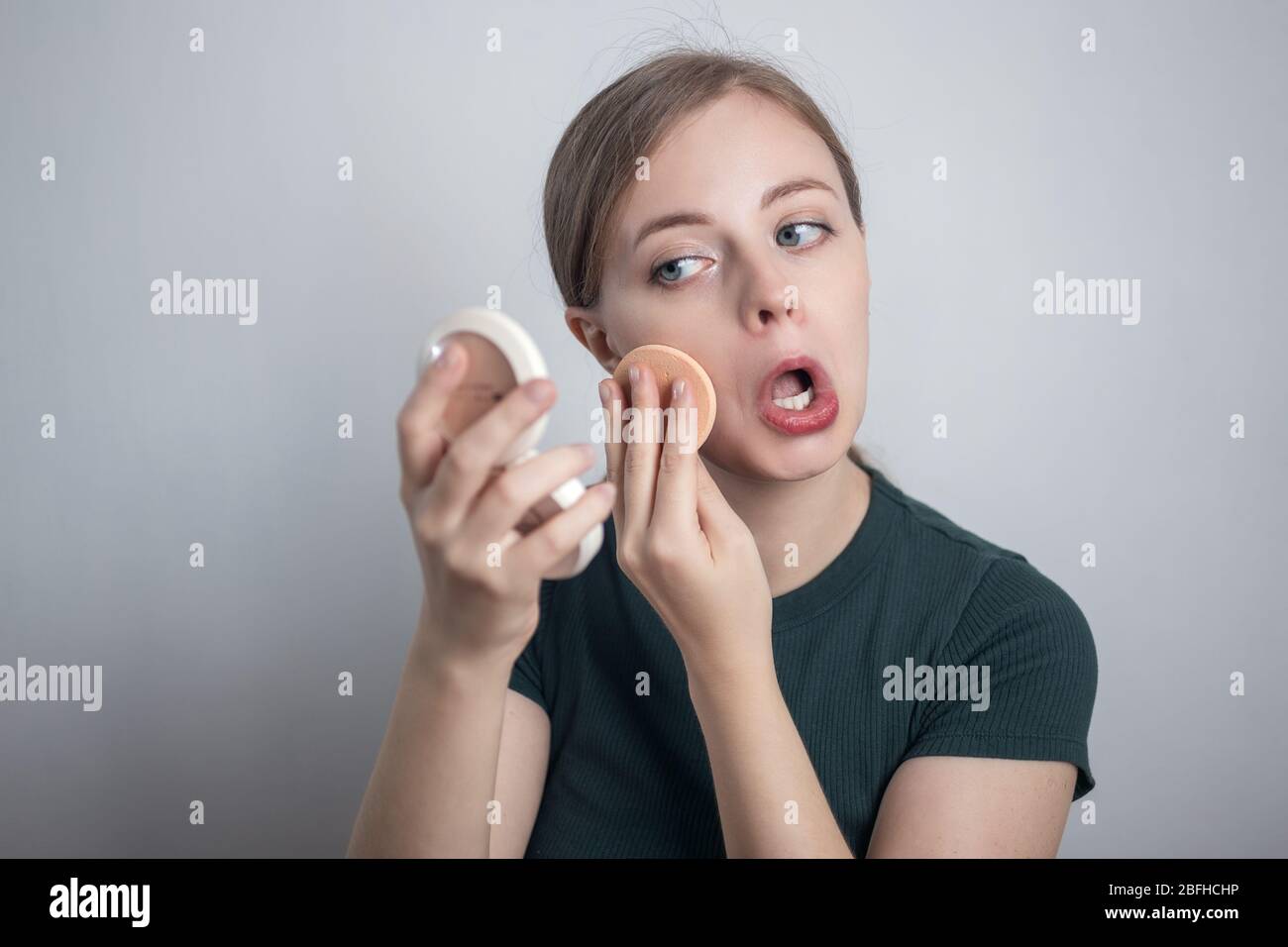 Young Caucasian woman girl is putting her make up powder foundation ...