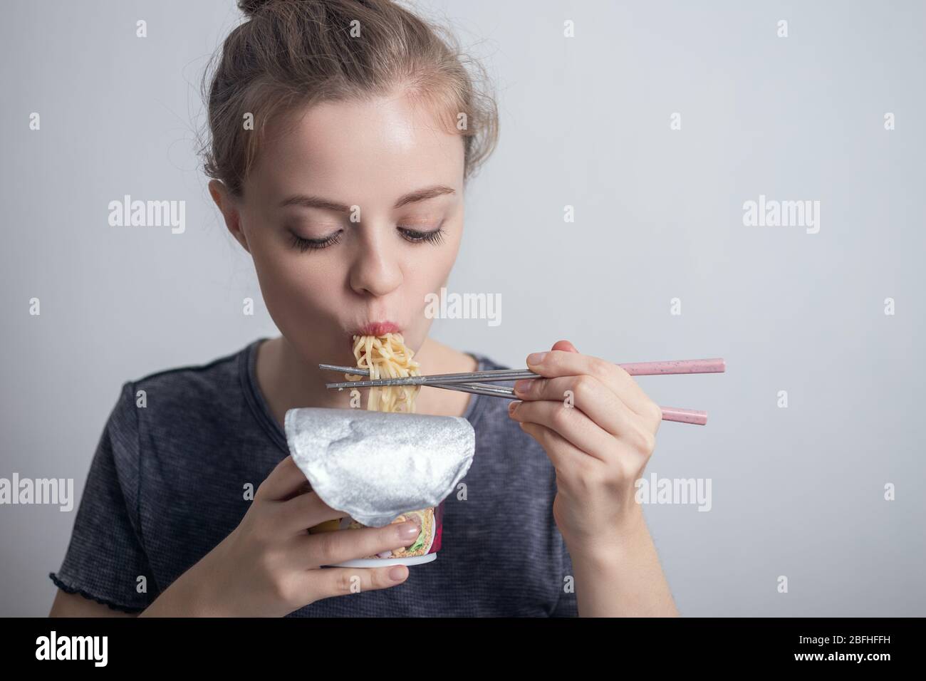 Young caucasian girl woman eating instant noodles ramen with chopsticks ...