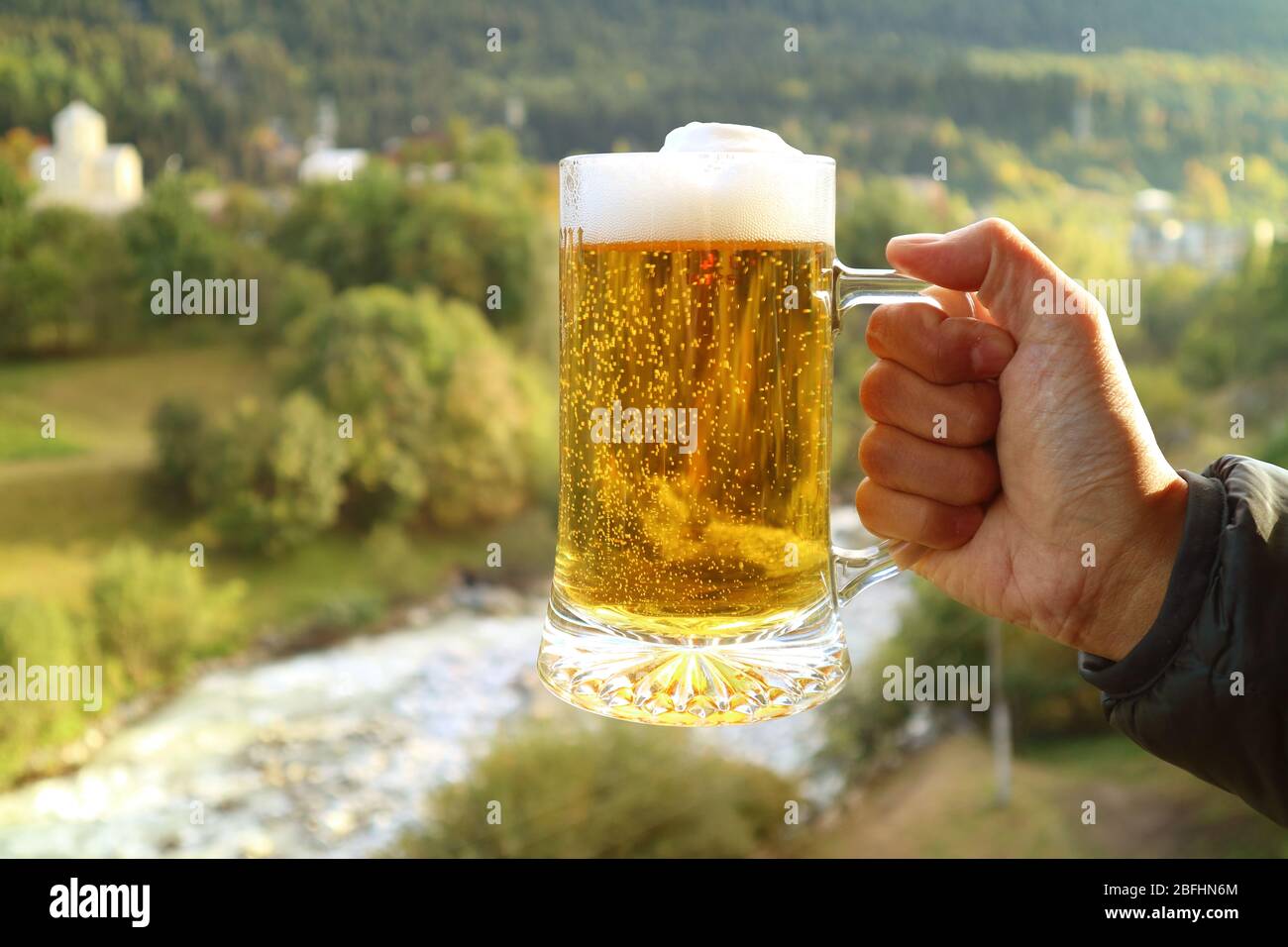 Pint of beer in man's hand against blurry foothill forest view in the ...