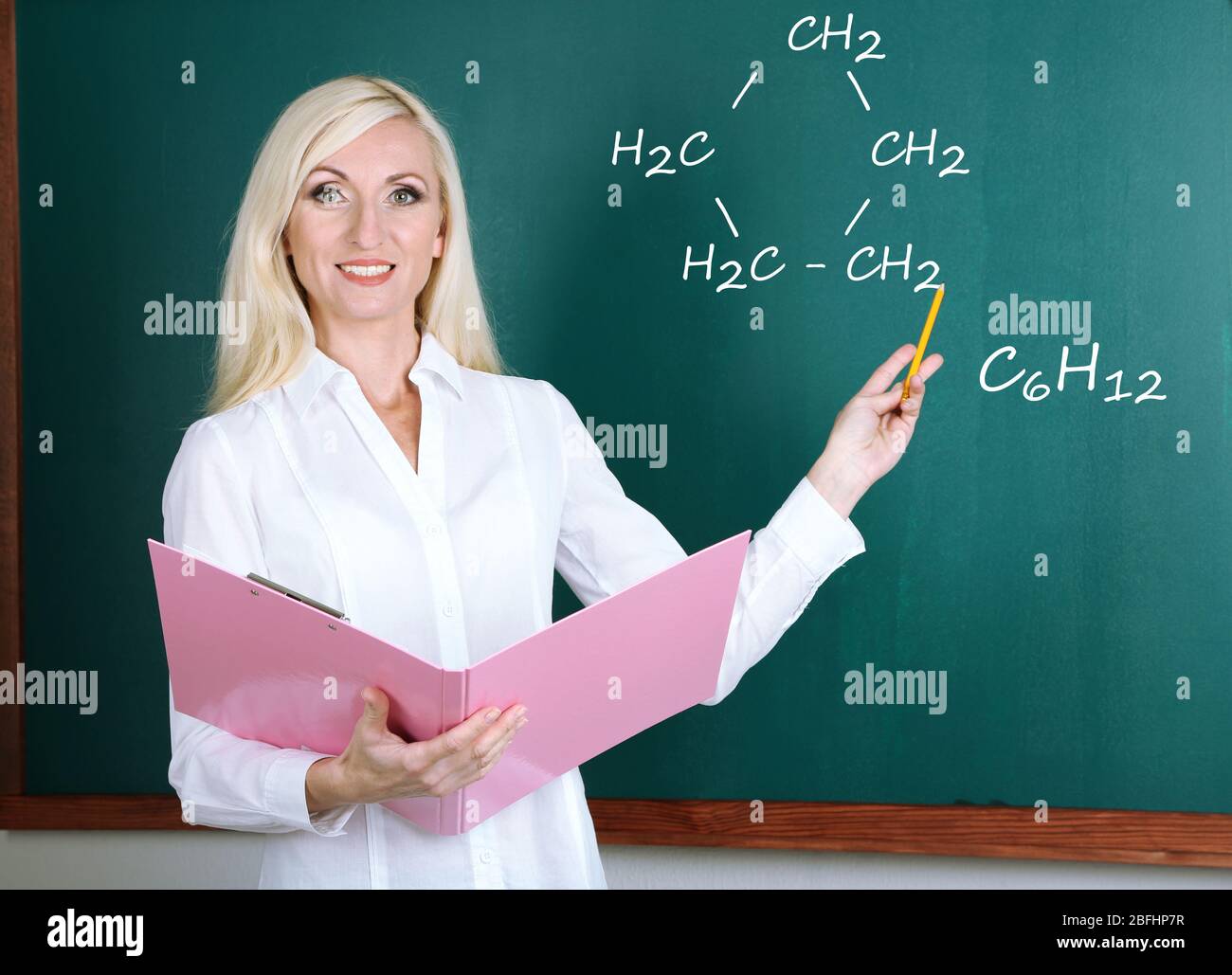 Chemistry teacher explaining formula written on blackboard to her ...