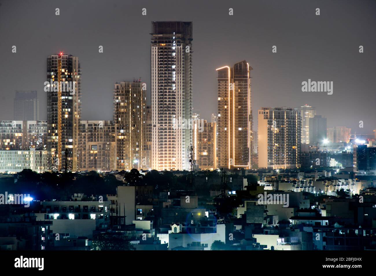 High rise multi story skyscrapers lit up at night with small houses in ...