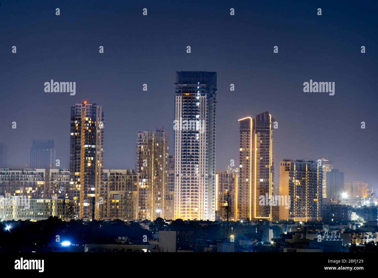 High rise multi story skyscrapers lit up at night with small houses in ...