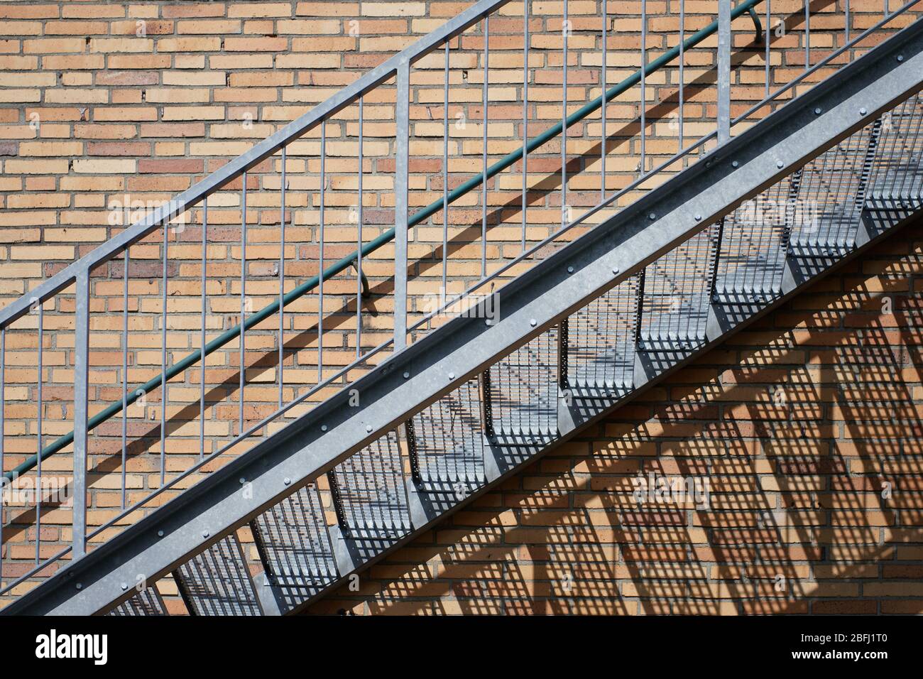 Exterior steel staircase on a red brick building wall with harsh shadow ...
