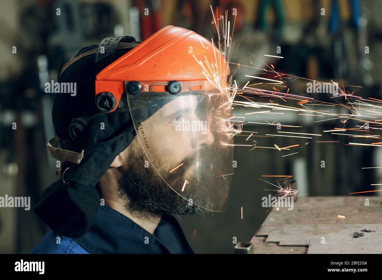Man worker in transparent protective mask works on metal with circular ...