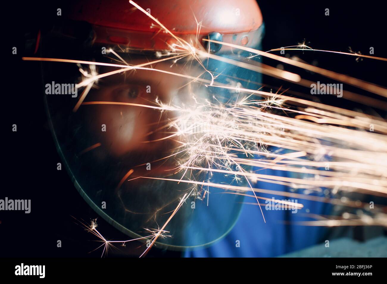 Man worker in transparent protective mask works on metal with circular ...