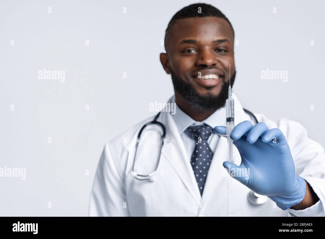 Smiling black doctor with stethoscope holding an injection Stock Photo ...