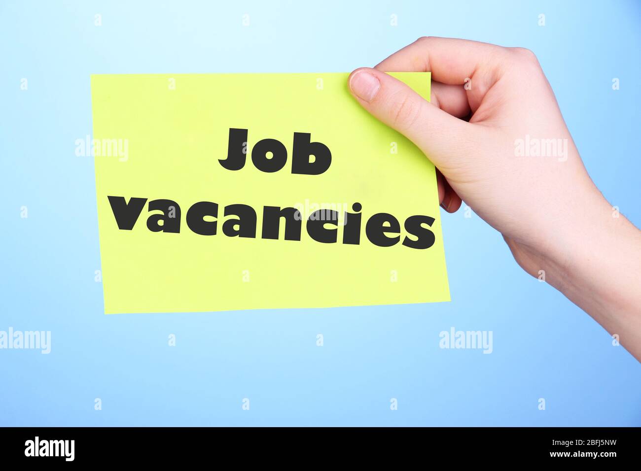Job Vacancies text on piece of paper in hand on blue background Stock ...