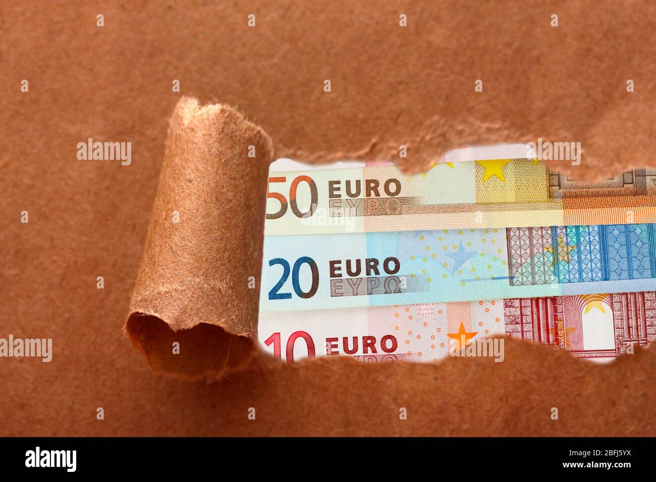 Euro banknotes through torn craft paper Stock Photo - Alamy