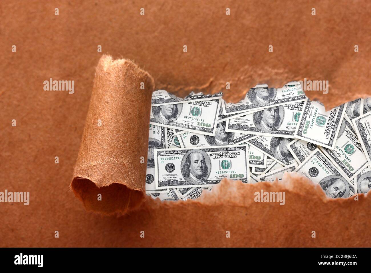 Dollars through torn craft paper Stock Photo - Alamy