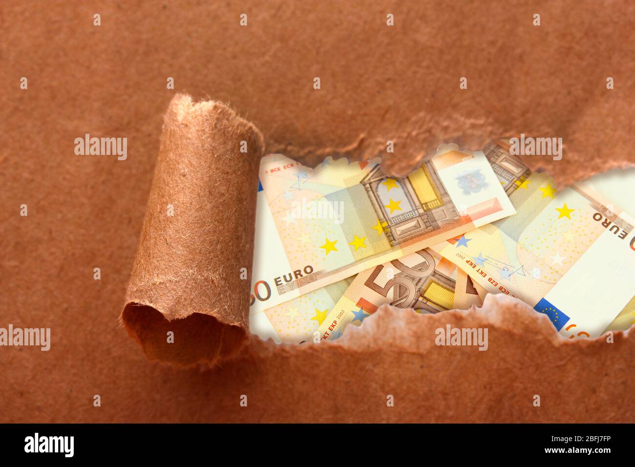 Euro banknotes through torn craft paper Stock Photo - Alamy