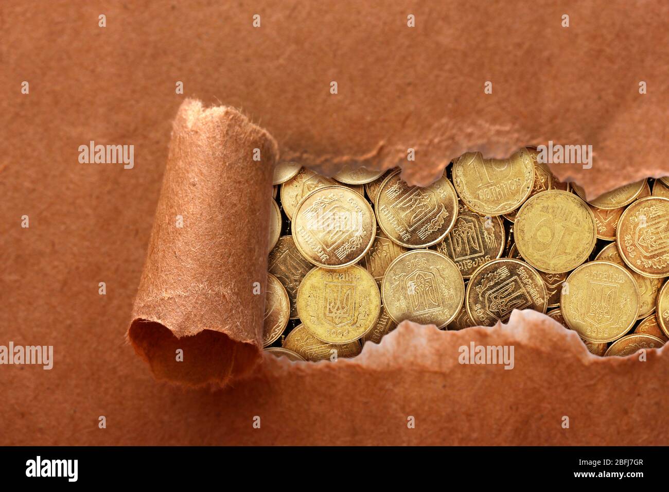 Golden coins through torn brown paper Stock Photo - Alamy