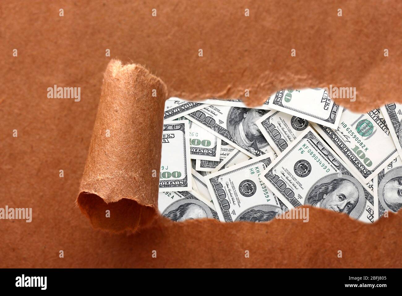 Dollars through torn craft paper Stock Photo - Alamy