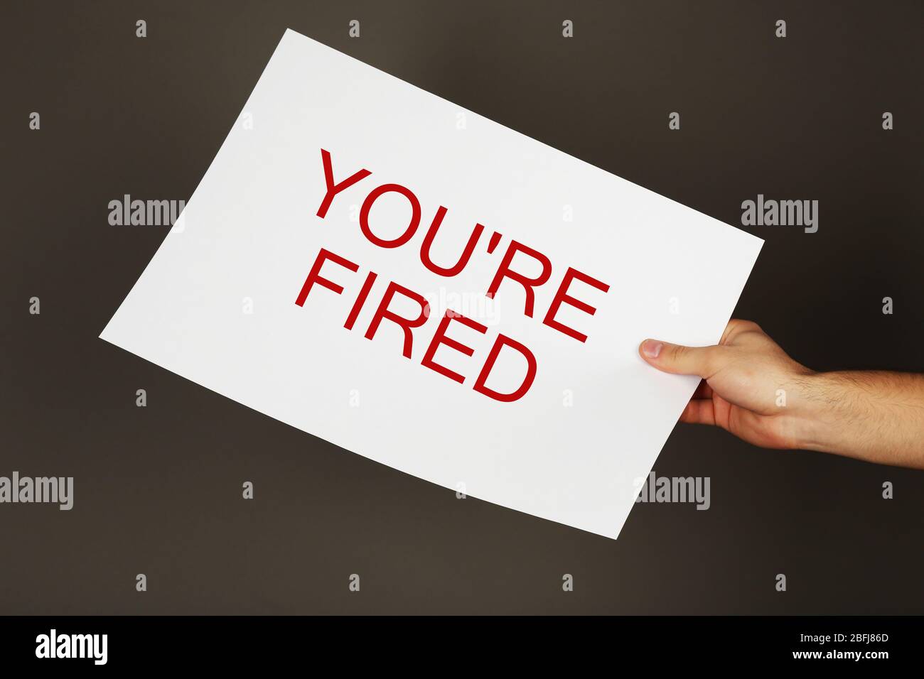 Sheet of paper with text You're Fired in male hand on dark background ...