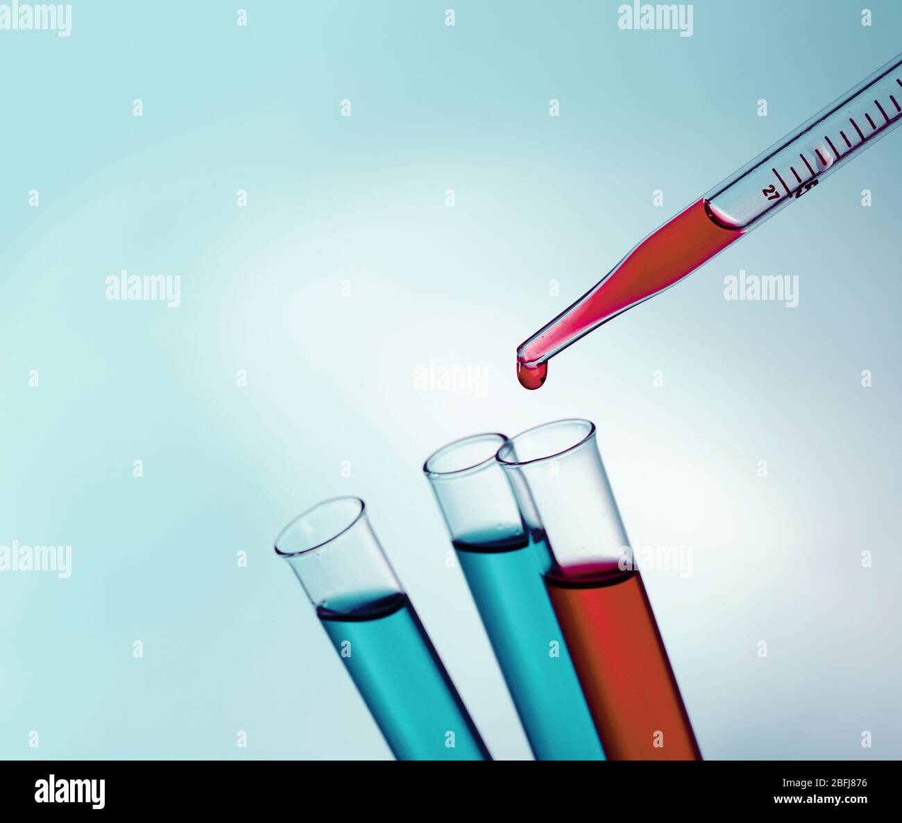 Pipette adding fluid to the one of test-tubes on light background Stock ...