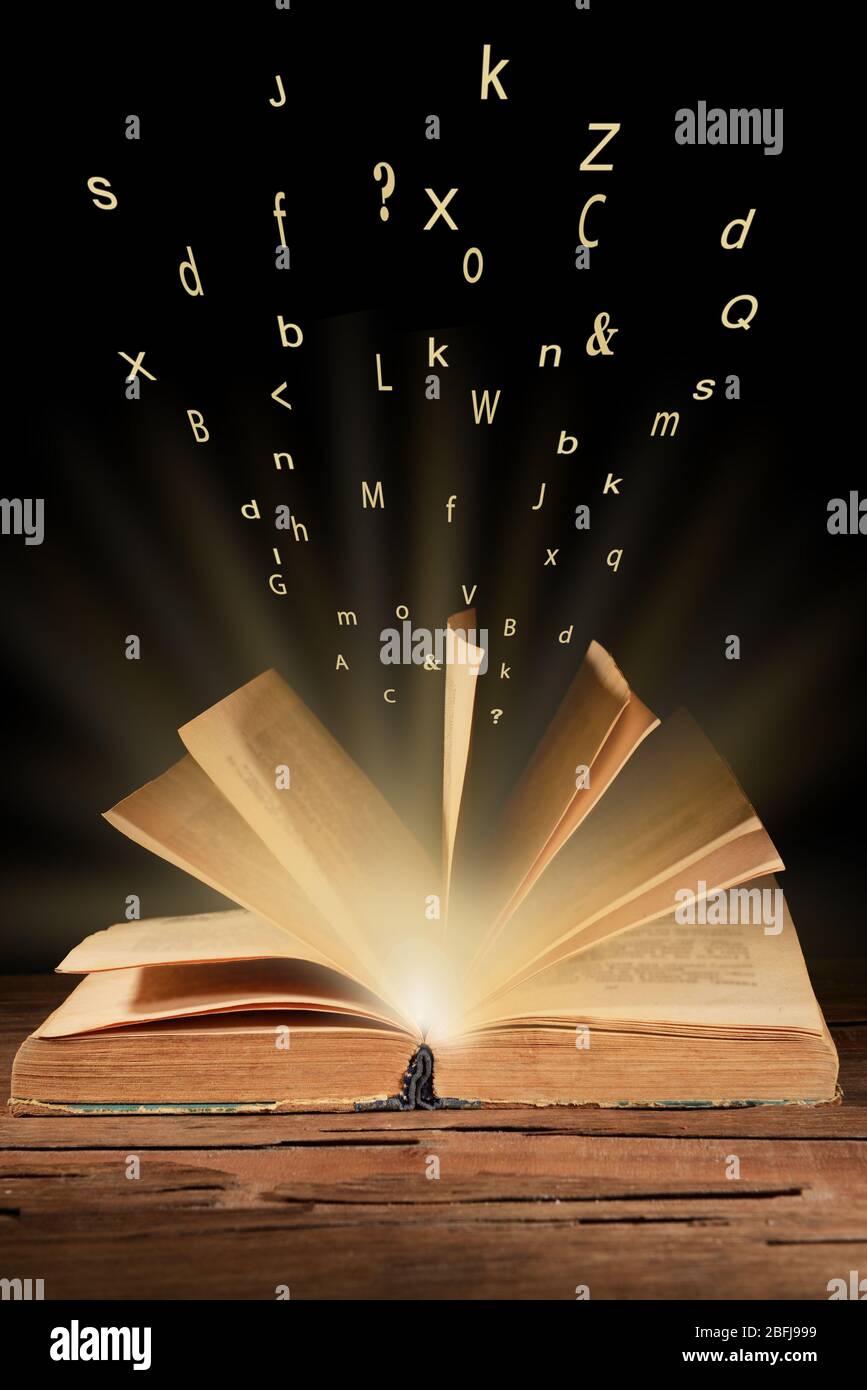 Open book with flying letters on table on dark background Stock Photo ...