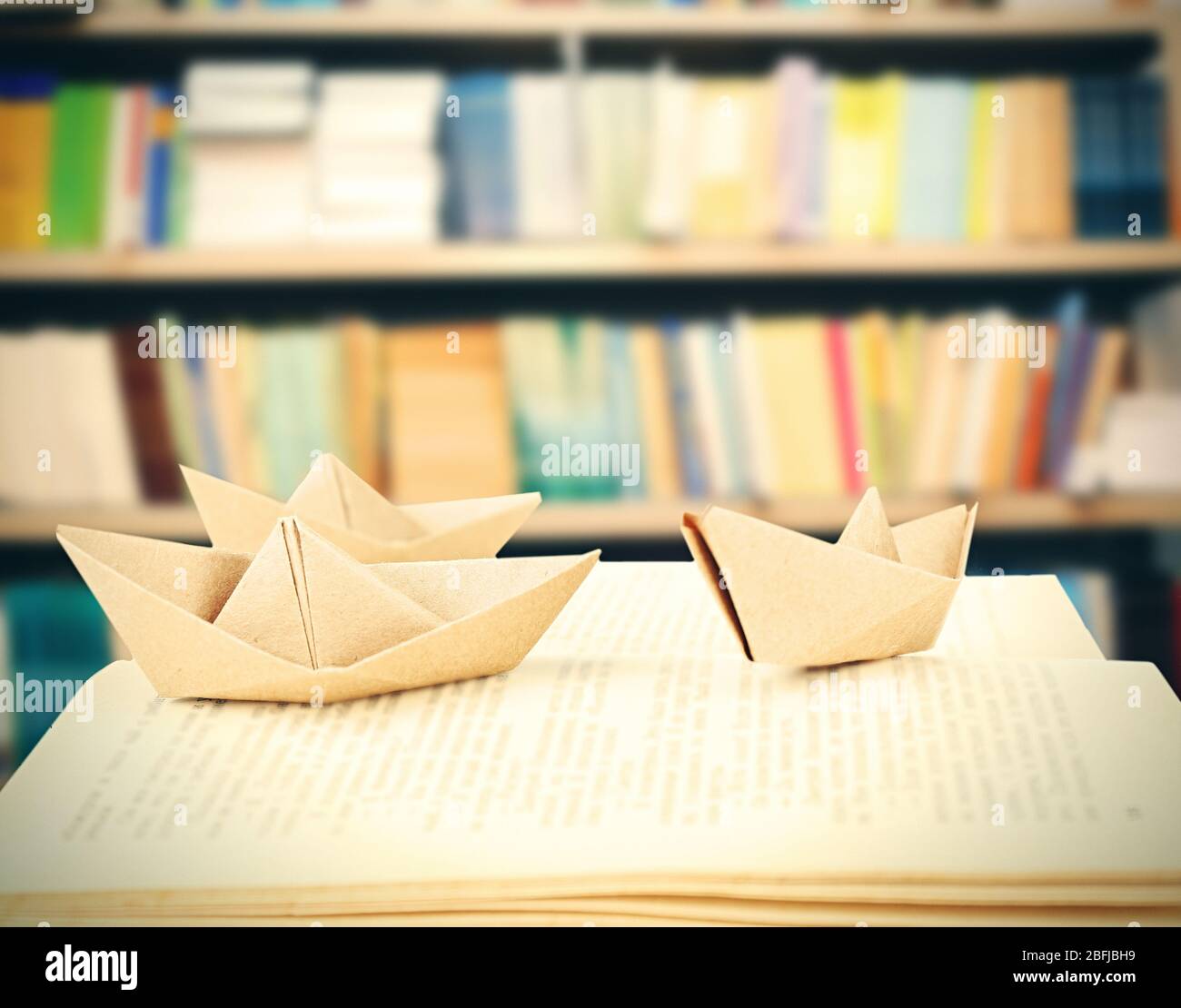 Open book with paper ships on bookshelves background Stock Photo - Alamy