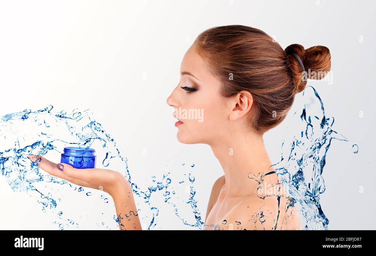 Beautiful young woman with moisturizing cream and water splash isolated ...