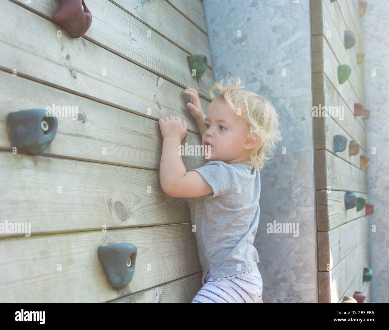 Portrait of cute blonde girl climbing plastic boulder wall outdoor ...