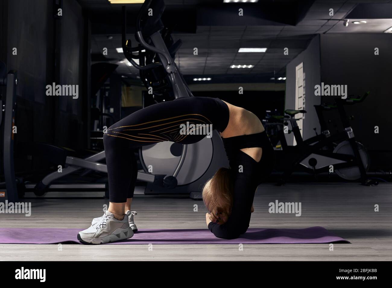 Sporty girl does stretching exercises in gym stands on the bridge ...