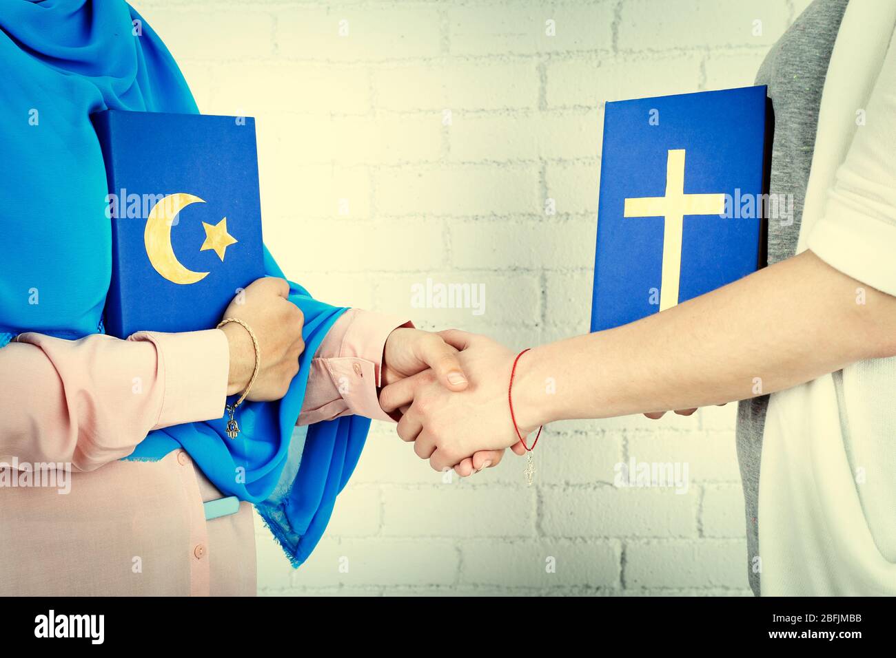 Two friends holding books with religions symbols Stock Photo - Alamy