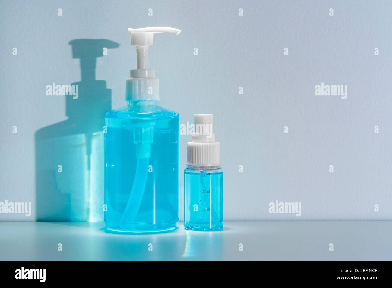 Bottles of blue anti-septic alcohol hand gel and spray on white table and casting blue shadow on ...