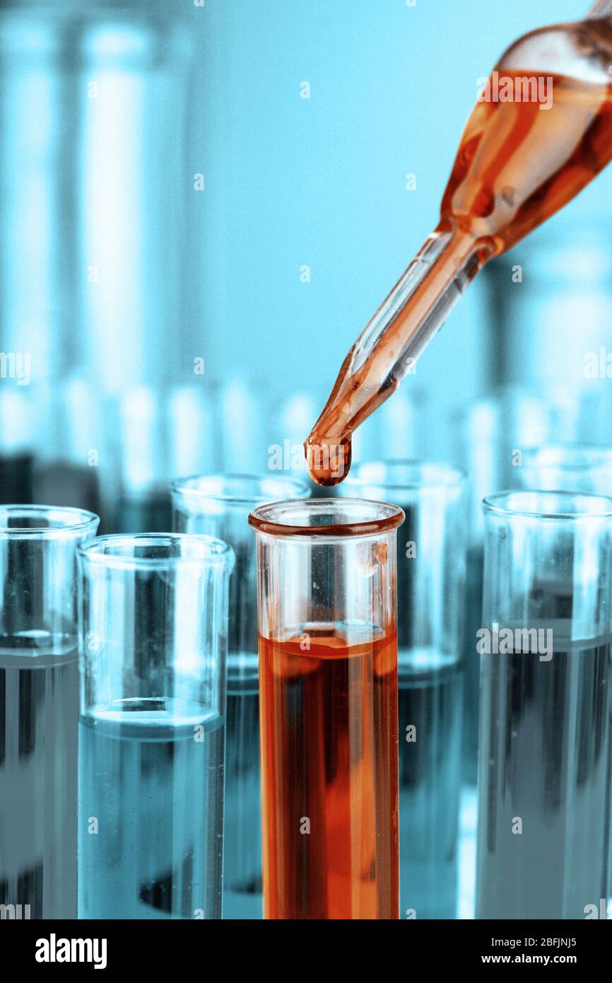 Laboratory pipette with drop of color liquid over glass test tubes ...