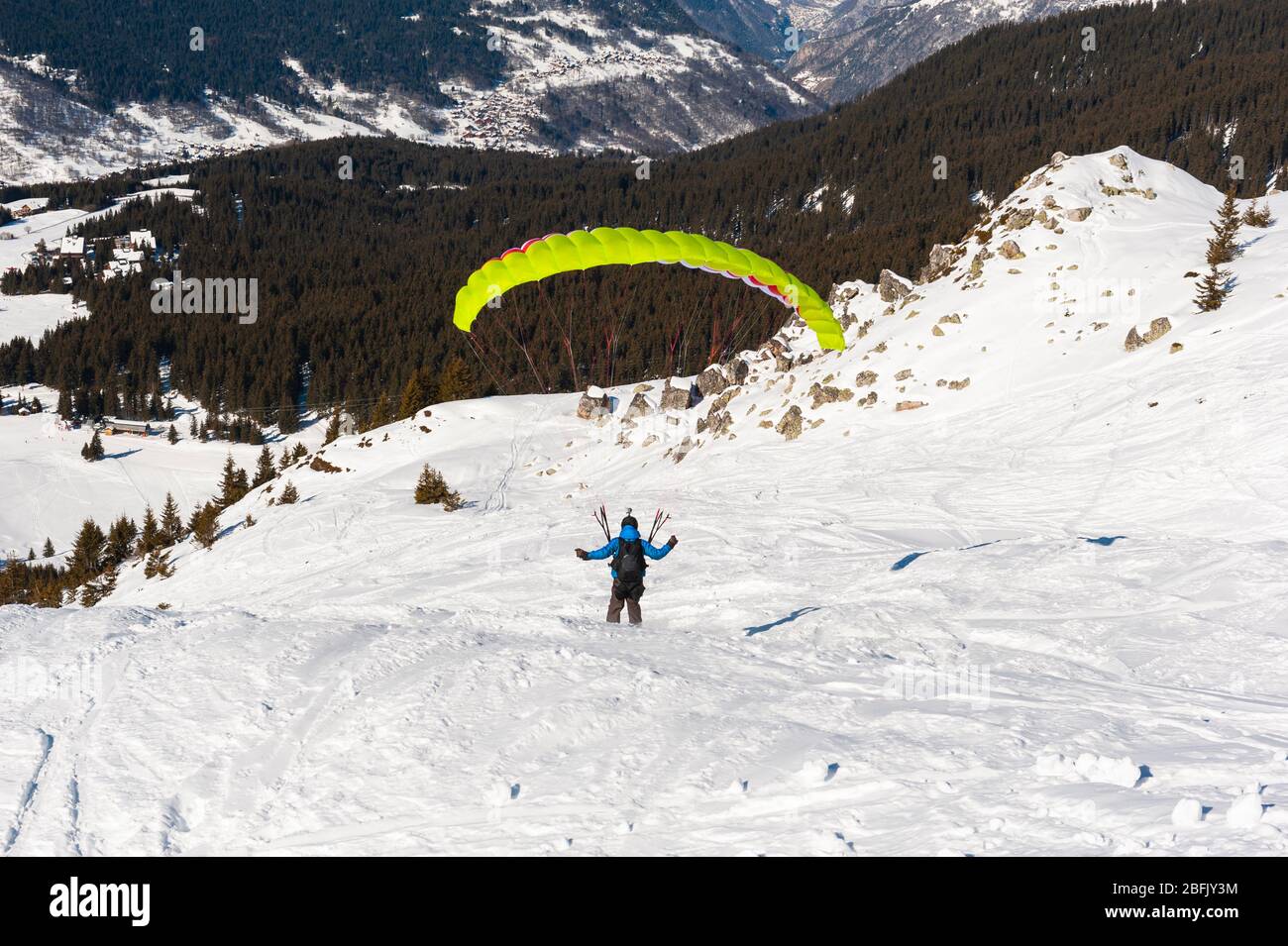Paraglider taking off from a snow covered slope looking down an alpine ...