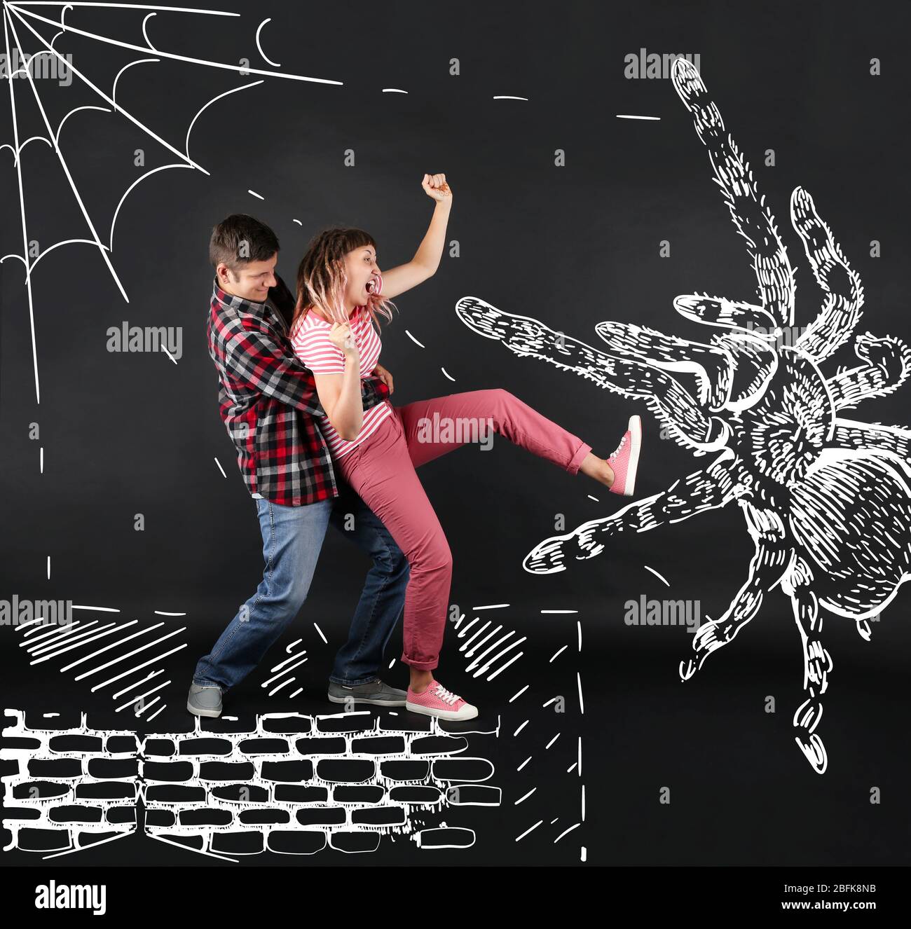 Funny young couple fighting with a big spider, on black background ...
