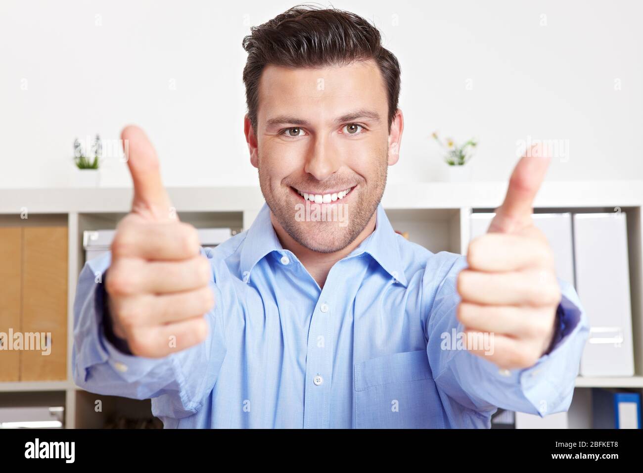 Laughing manager in the office holds his two thumbs up Stock Photo - Alamy