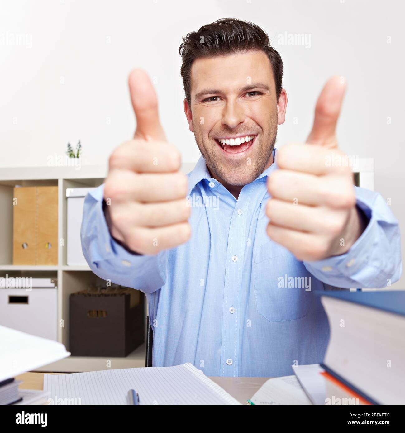 Cheering student at the desk holds both thumbs up Stock Photo - Alamy