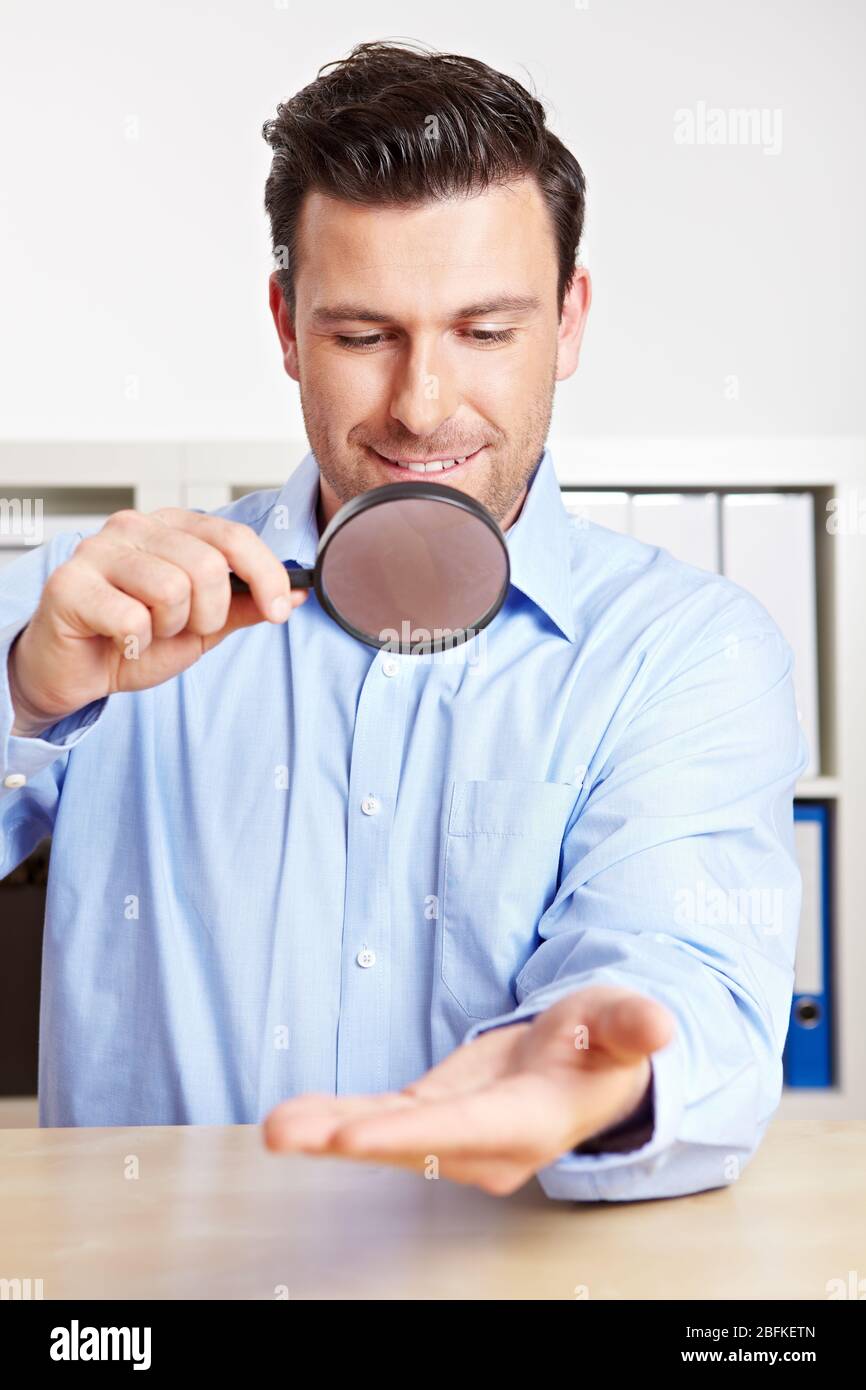 Businessman in the office looks with a magnifying glass at an empty ...