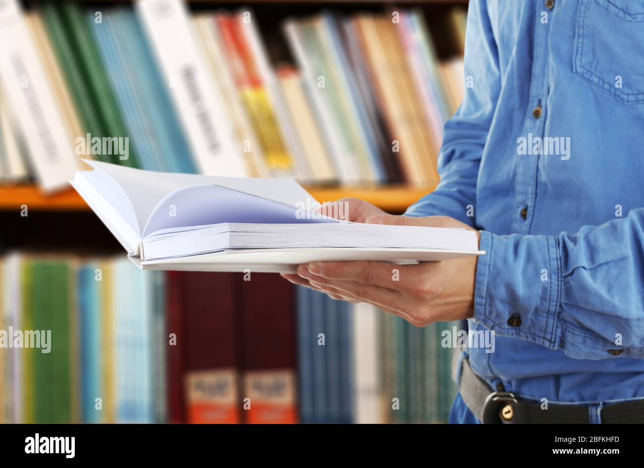 Male hands holding open book on bookshelves background Stock Photo - Alamy
