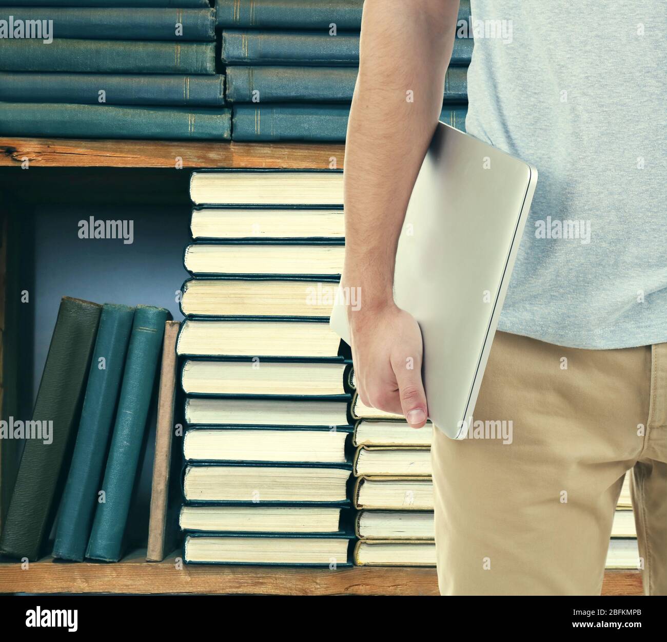 Male hand holding laptop on bookshelves background Stock Photo - Alamy