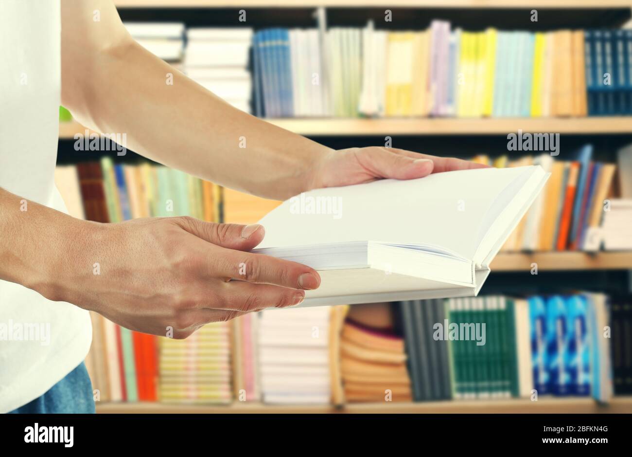 Male hands holding open book on bookshelves background Stock Photo - Alamy