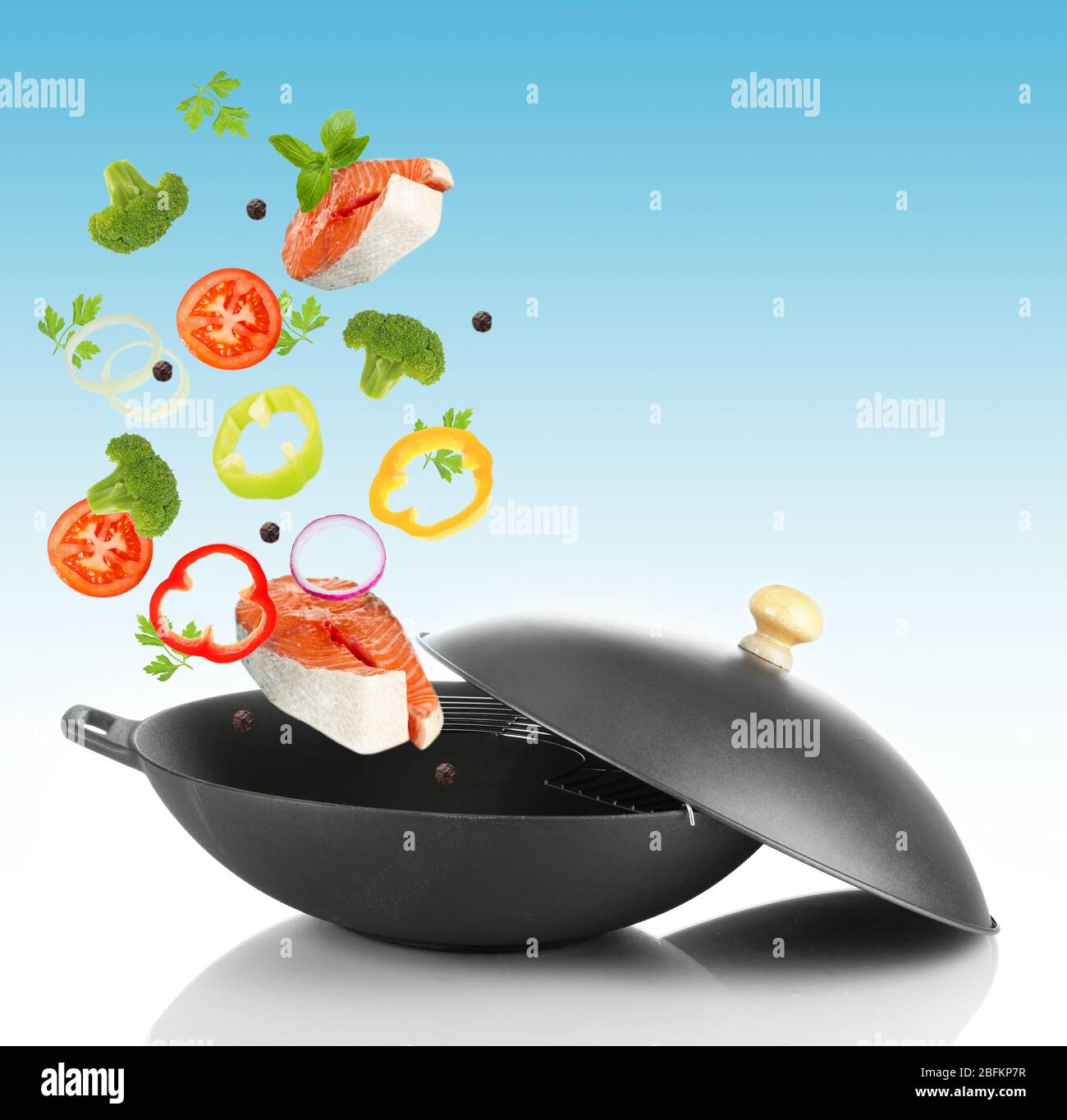 Fresh vegetables falling in the frying pan on light blue background ...