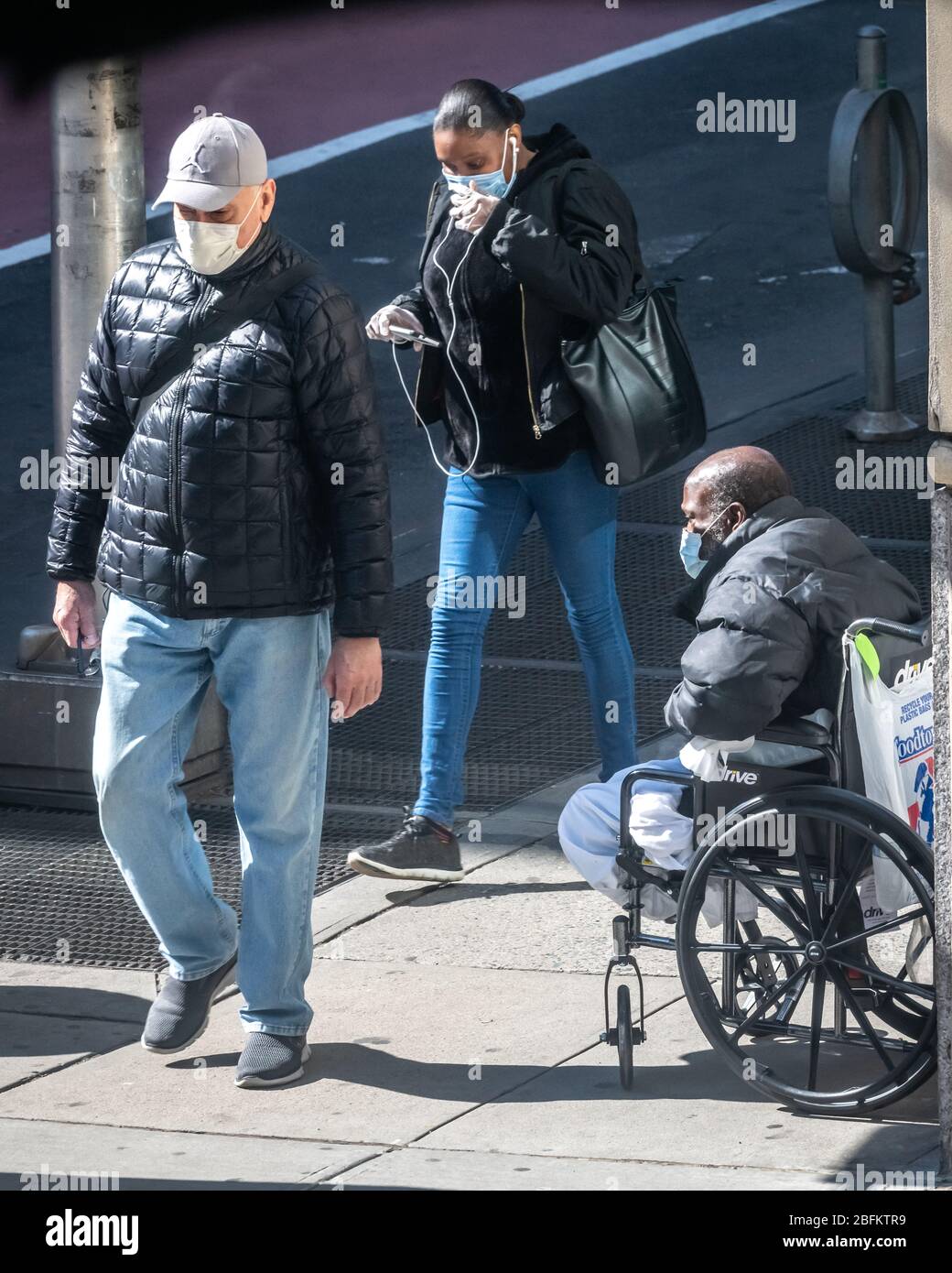 New York, USA. 19th Apr, 2020. Wearing face masks, people walk past a ...