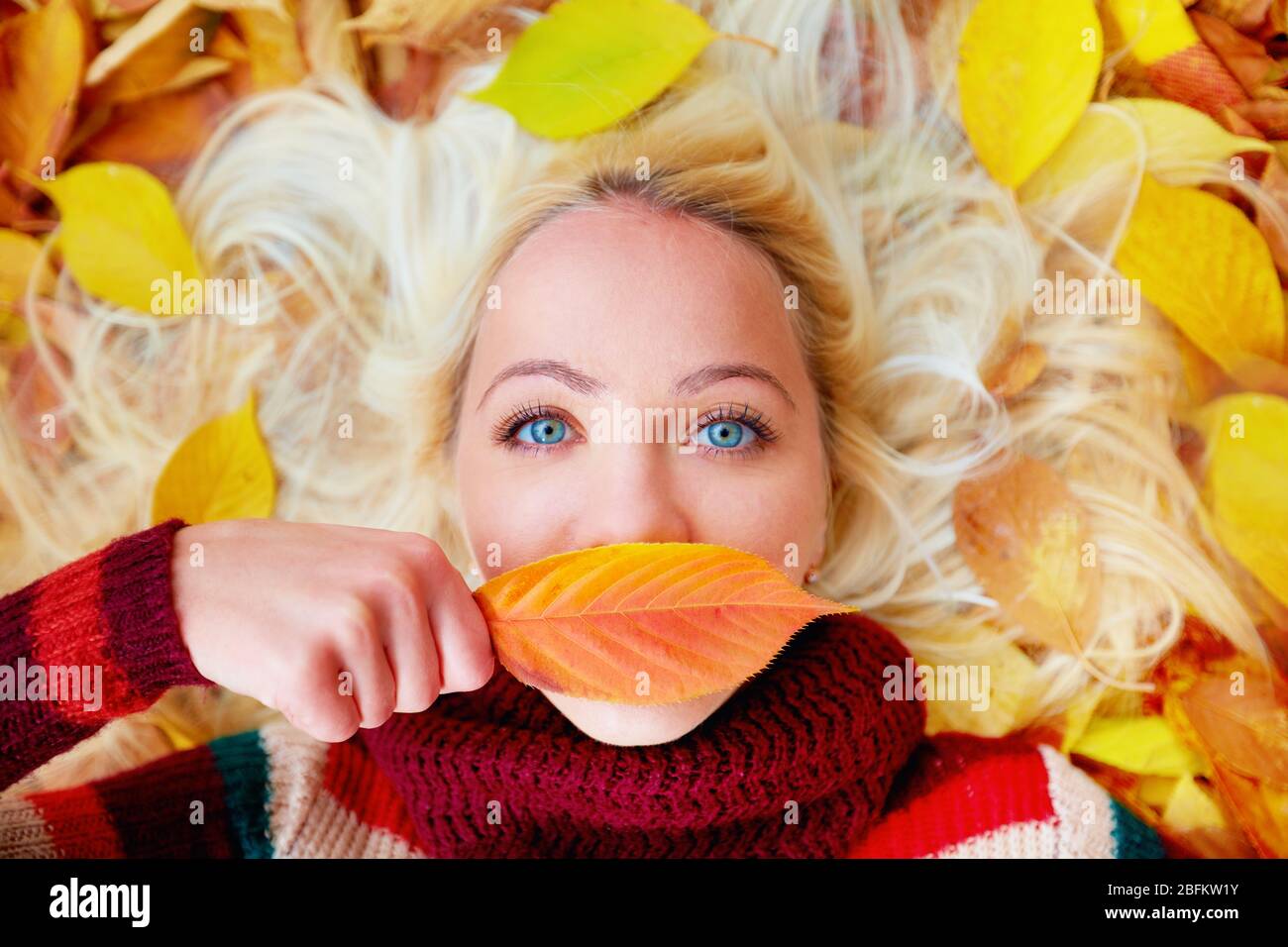 young girl lying among autumn leaves, hiding lips behind a leaf Stock ...