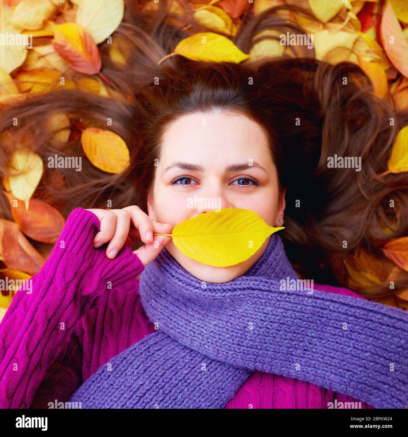 young girl lying among autumn leaves, hiding lips behind a leaf Stock ...