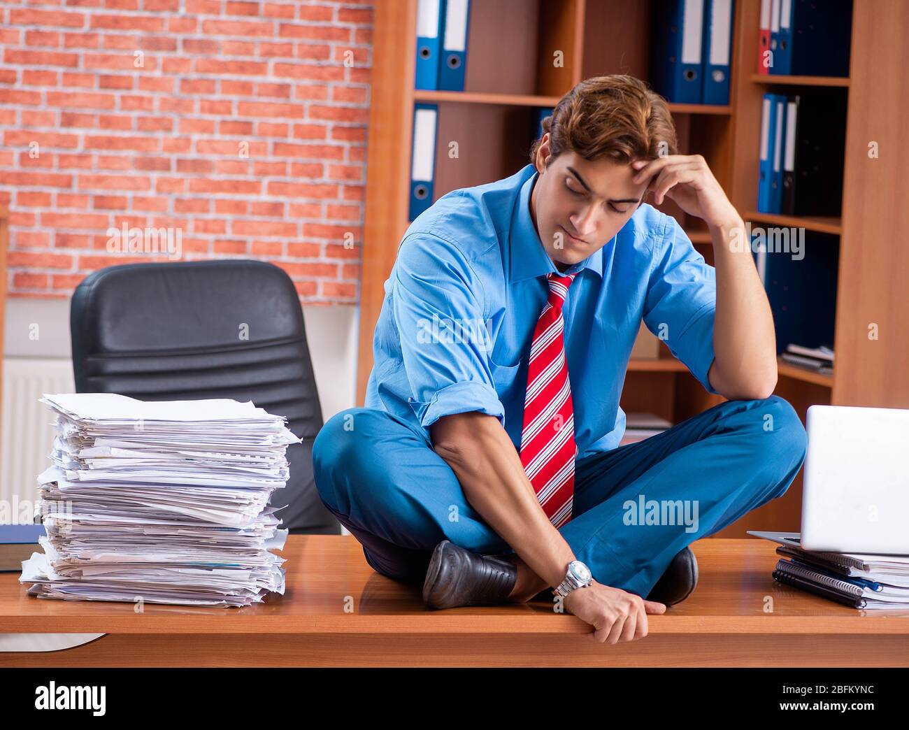 The young employee with excessive work sitting at the office Stock ...