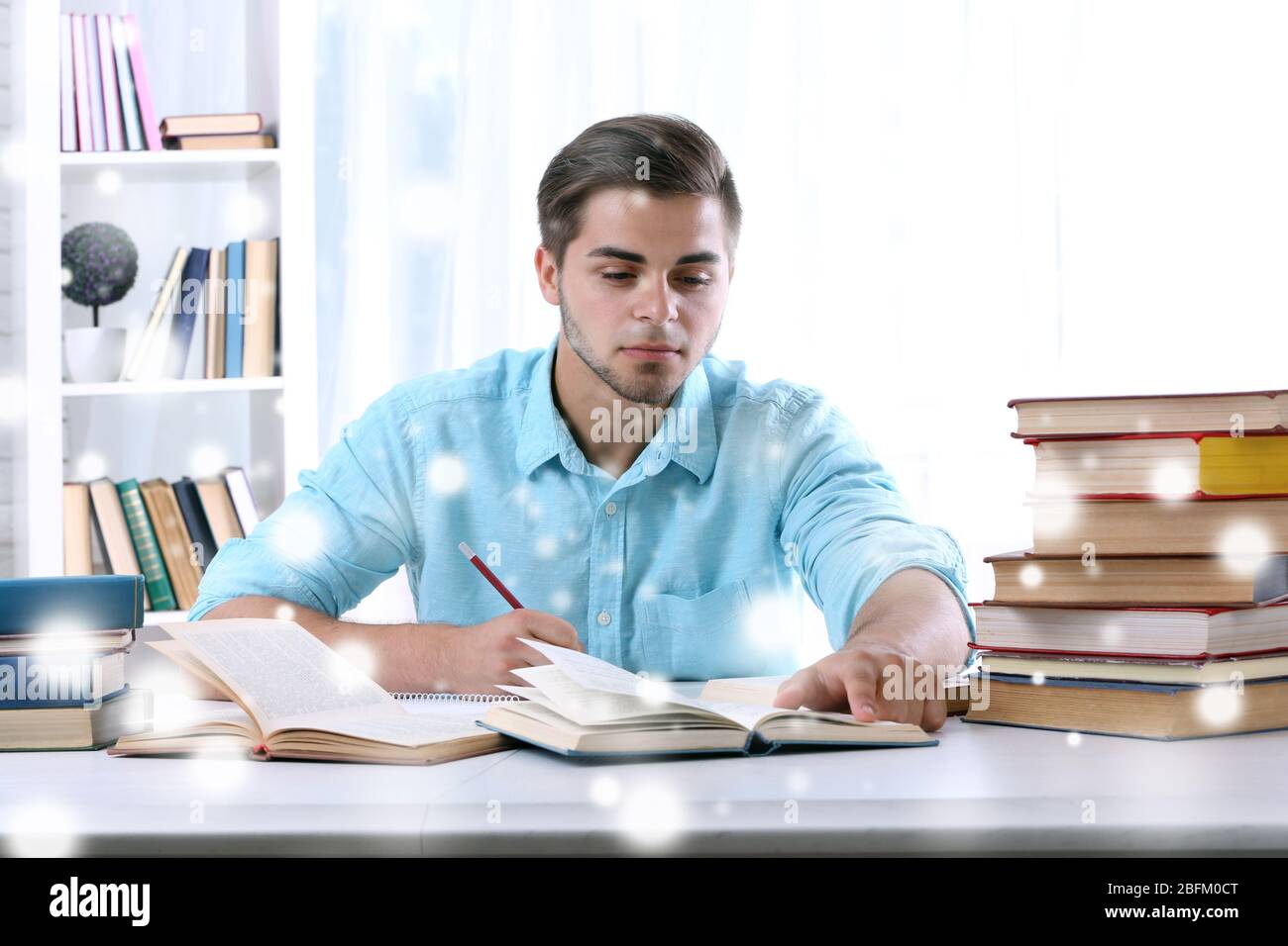Young man reading book at table in room over snow effect Stock Photo ...