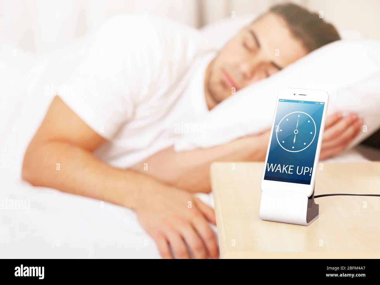 Young man waking up with mobile alarm clock Stock Photo - Alamy