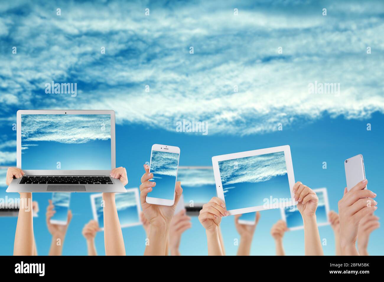 Hands holding electronic gadgets with sky on screens. Cloud computing ...