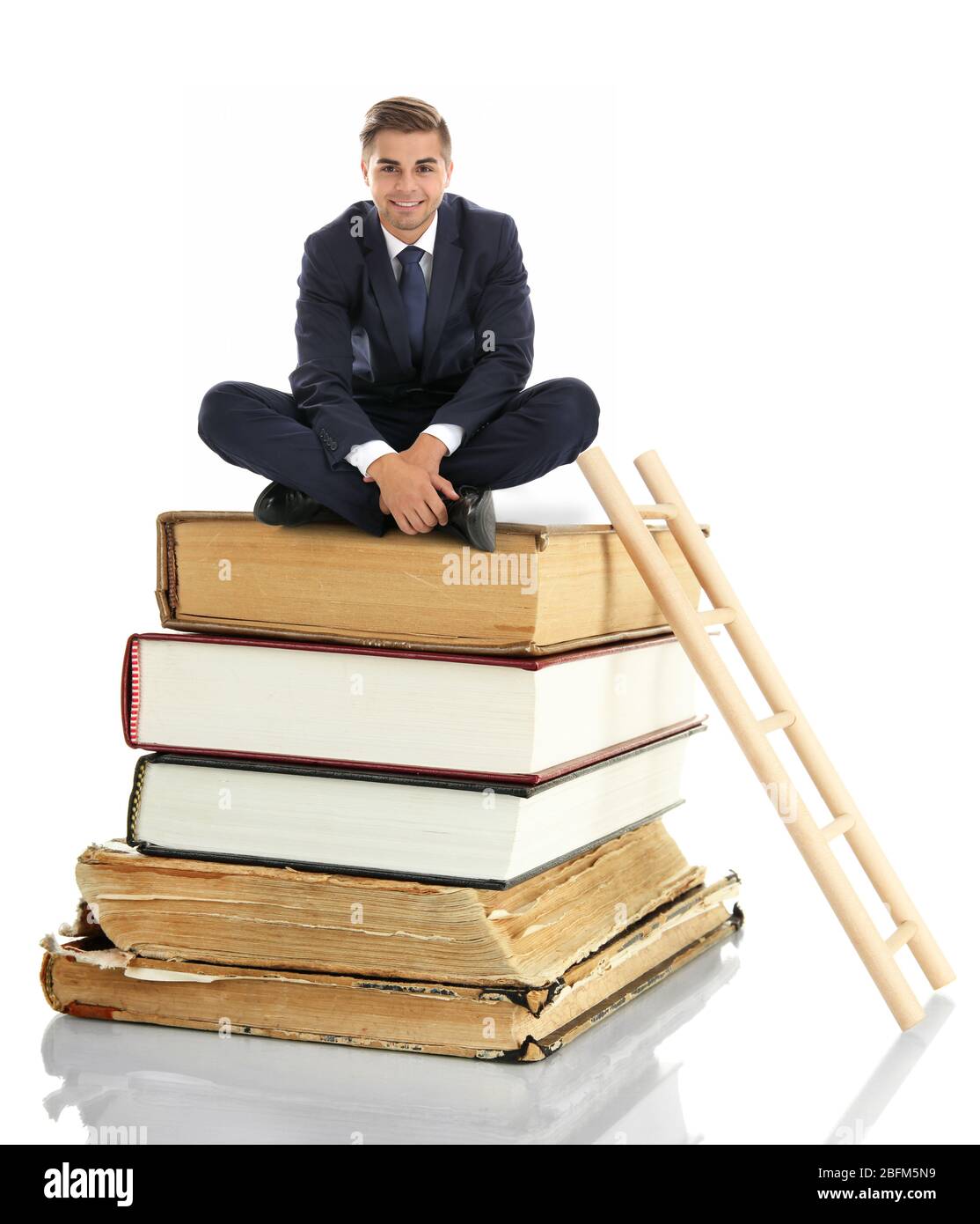 Handsome young man sitting on stack of books isolated on white Stock ...