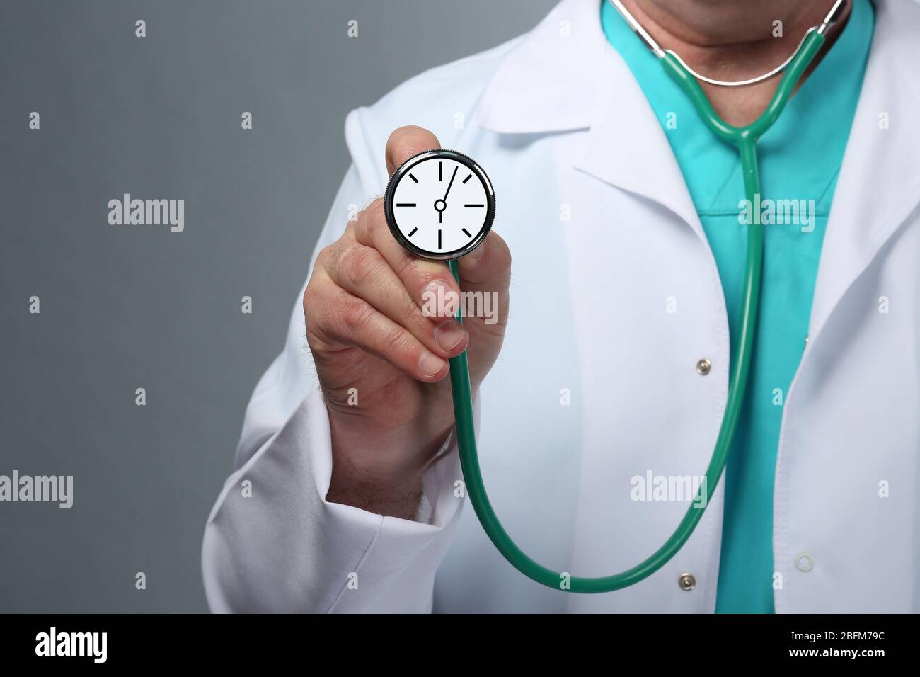 Male doctor holding stethoscope with clock Stock Photo - Alamy